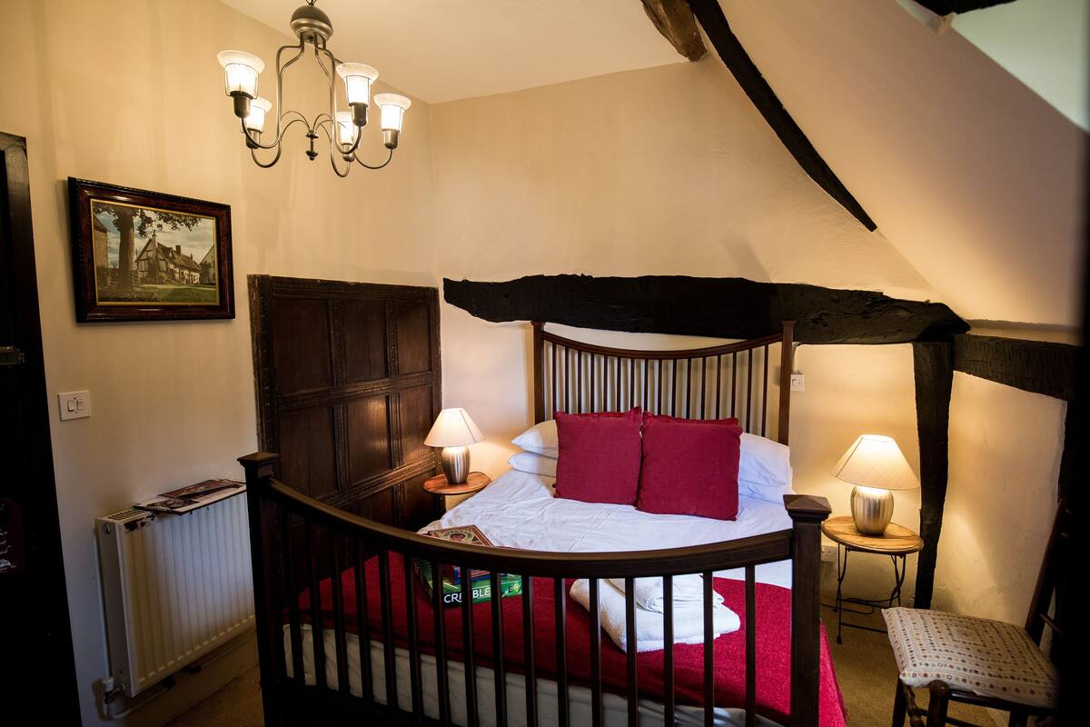 Quarto com uma cama de madeira com dossel, duas luminárias de cabeceira, um radiador, um quadro na parede e uma cadeira.