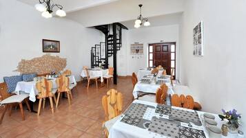 Uma sala de jantar com várias mesas e cadeiras, uma escada e uma parede decorada com quadros.