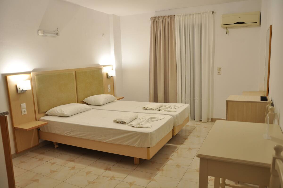 Quarto de hotel com duas camas, uma mesa e uma cadeira.
