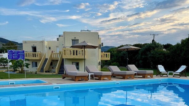 Uma piscina com espreguiçadeiras, um edifício com design arquitetônico singular e um céu claro.