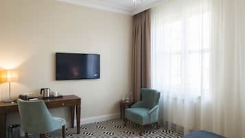 Quarto de hotel com televisão de tela plana na parede, uma escrivaninha com abajur, uma cadeira, uma cama e um tapete estampado.