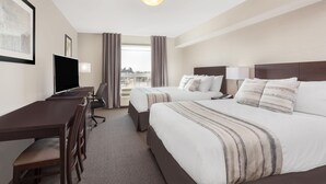 Quarto de hotel com duas camas, uma escrivaninha com cadeira, televisão e janela com cortinas.