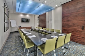 Uma sala de conferências com uma mesa comprida, cadeiras amarelas, um quadro branco e uma televisão na parede.