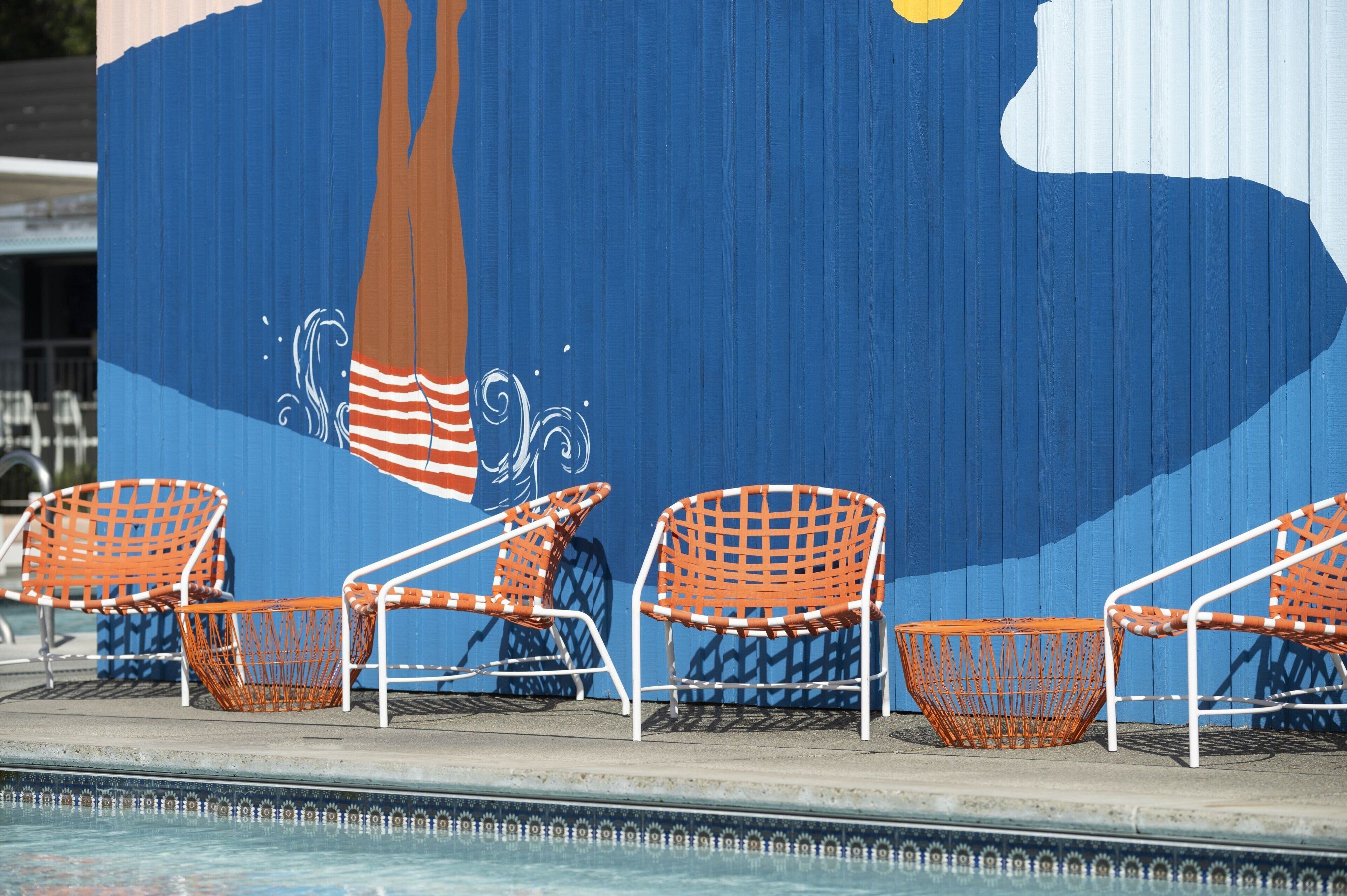 Uma área junto à piscina com cadeiras listradas em laranja e branco, e um mural azul com padrão de onda.