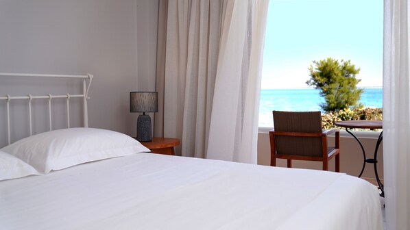 Quarto com cama, mesa de cabeceira, abajur, cadeira e vista para o oceano.