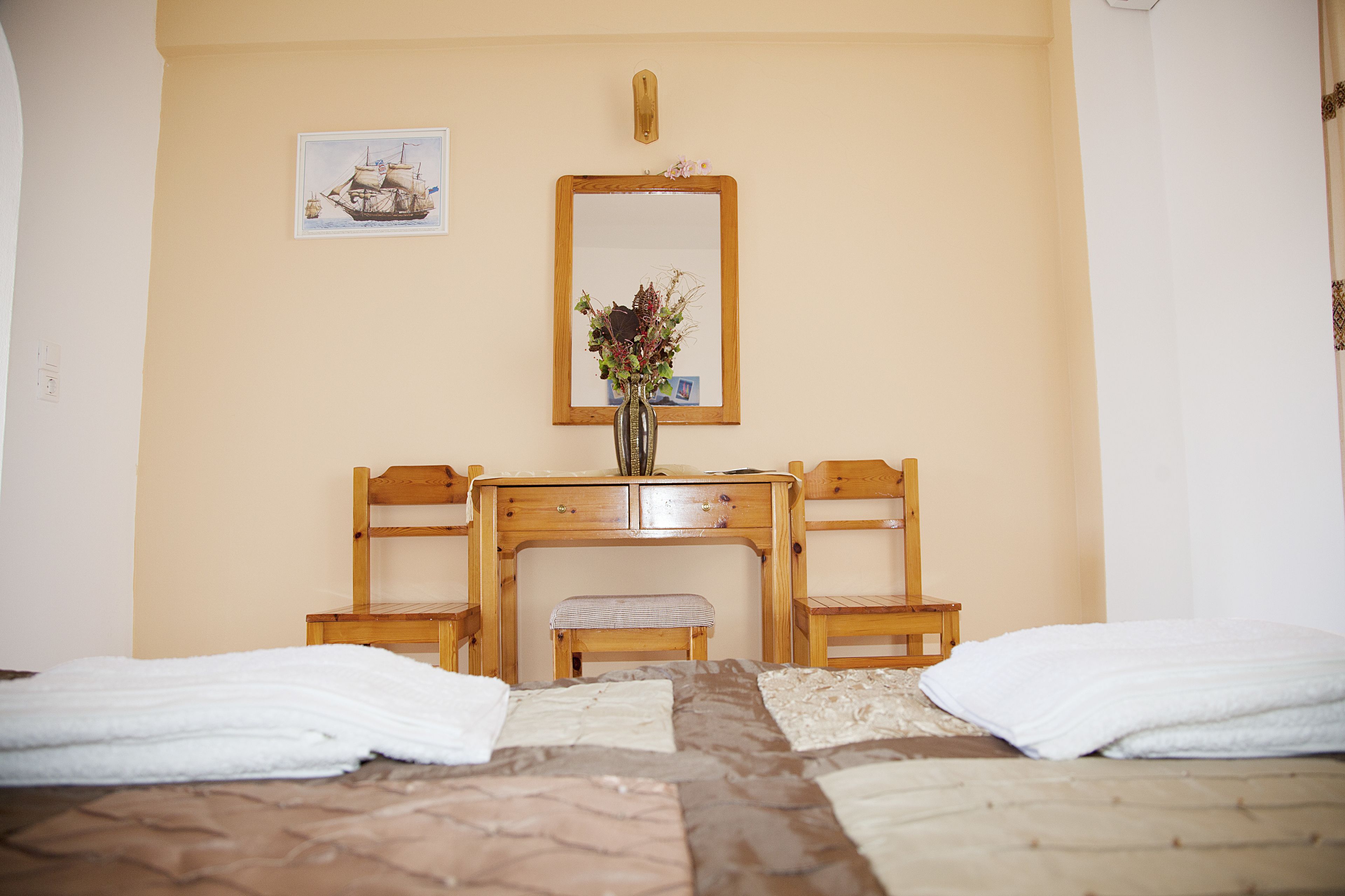 Quarto de hotel com uma escrivaninha de madeira, duas cadeiras, um espelho e um vaso com flores.