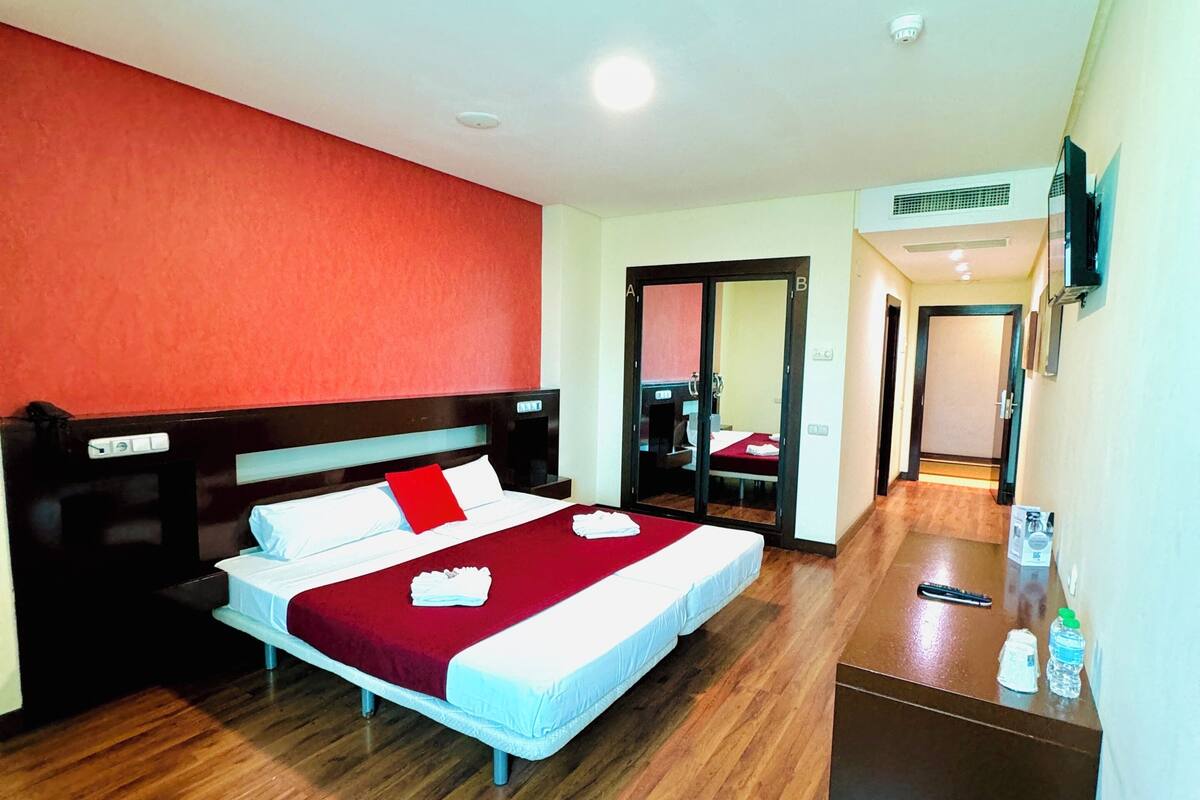 Quarto de hotel com cama, escrivaninha e televisão.