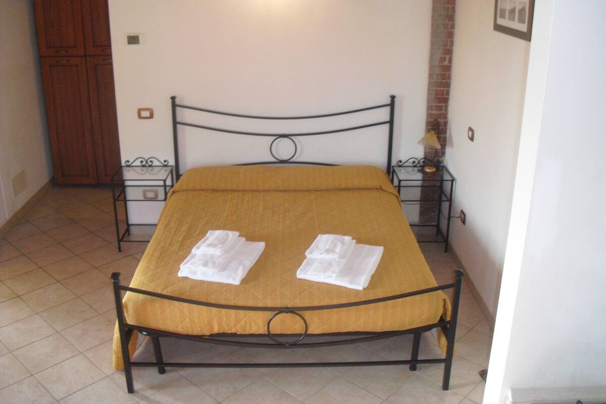 Uma cama de solteiro com estrutura metálica, um edredom amarelo e duas toalhas brancas sobre a cama.