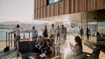 Um deck de madeira com mobiliário ao ar livre, com vista para um corpo d'água e o horizonte da cidade.