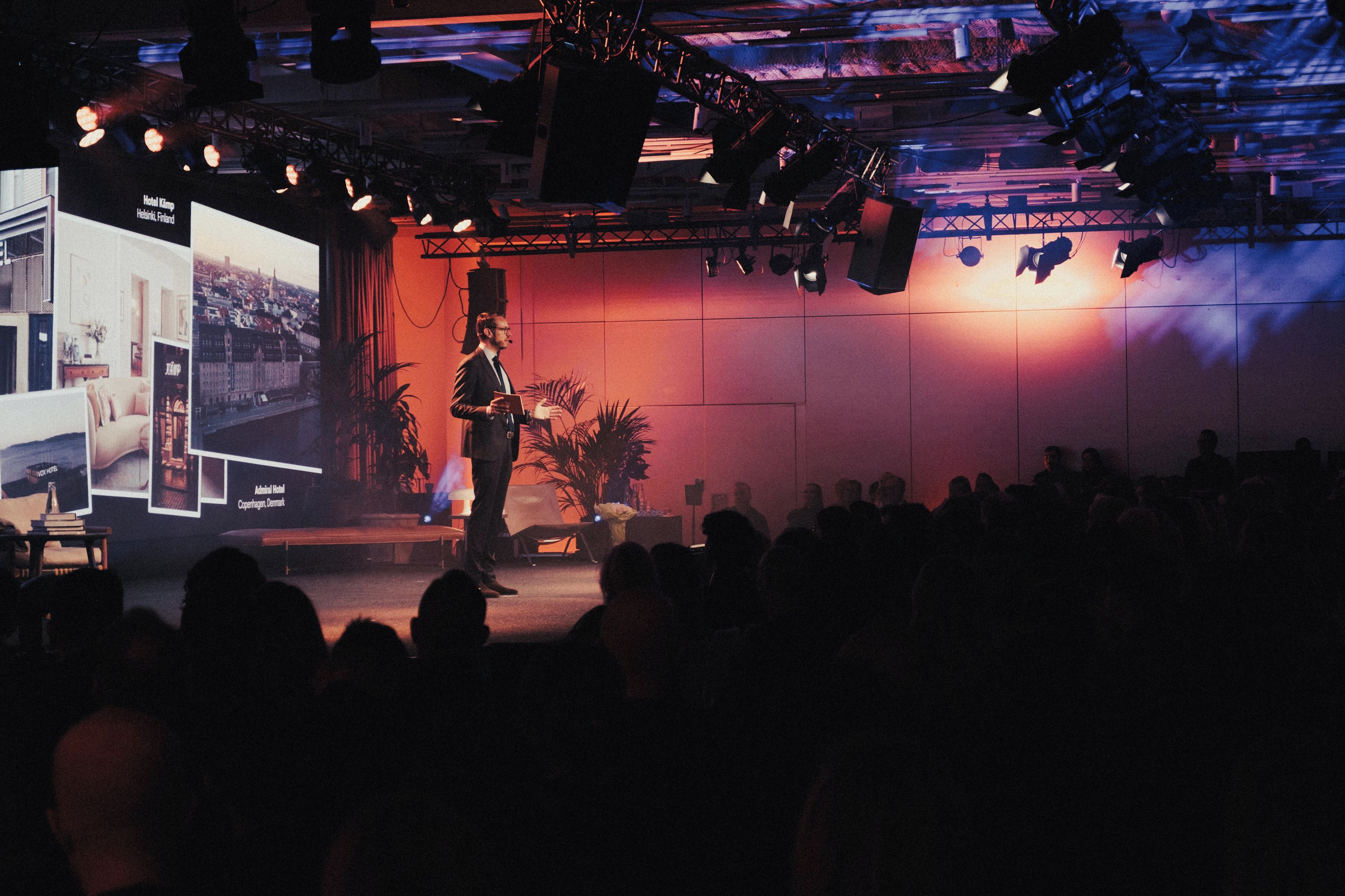 Palco com um orador e um ecrã grande a exibir informações sobre o hotel.