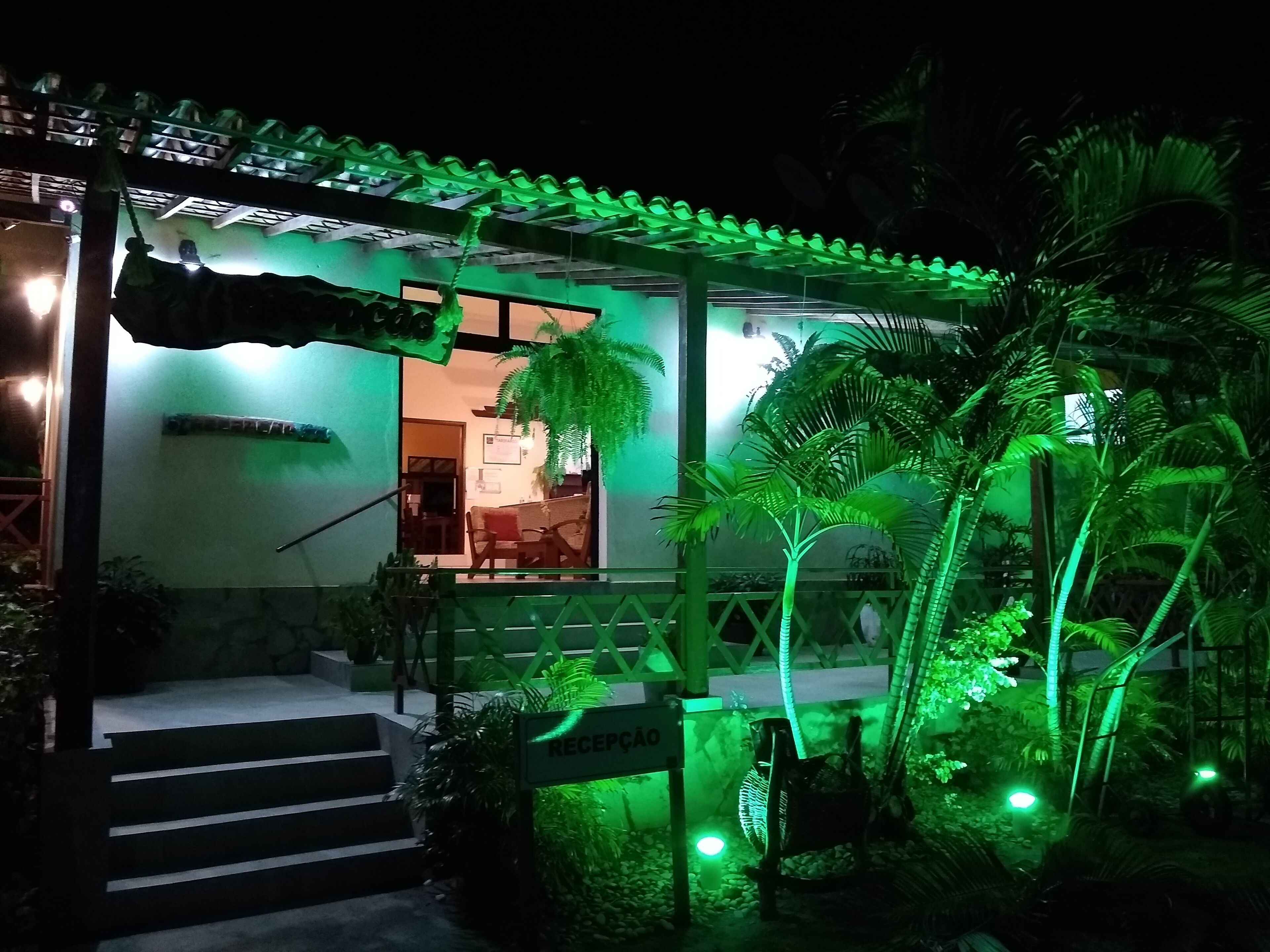 Entrada de edifício com pérgola iluminada em verde, área de recepção e escadaria.