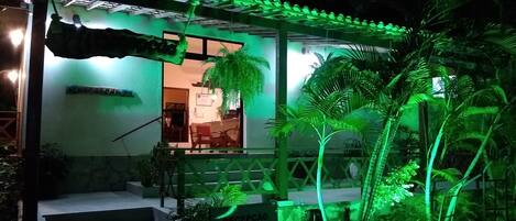 Entrada de edifício com pérgola iluminada em verde, área de recepção e escadaria.