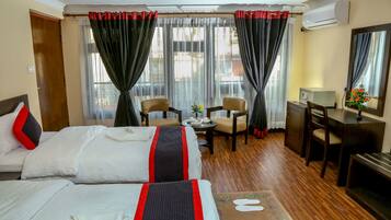 Quarto de hotel com duas camas, uma escrivaninha, uma cadeira, uma mesinha com uma planta e um ar condicionado.