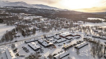 Vista aérea de uma cidade coberta de neve, com vários edifícios, incluindo uma grande instalação industrial com teto plano e algumas estruturas menores.
