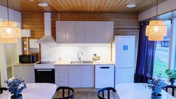 Cozinha moderna com armários brancos, micro-ondas, fogão e pia. Há duas luminárias pendentes e uma janela com cortinas.