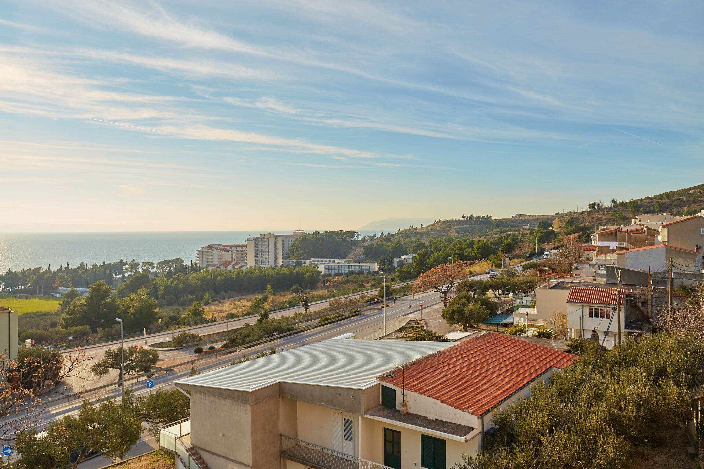 Uma área residencial costeira com edifícios, uma estrada e vista para o mar.