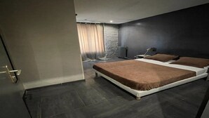 Quarto moderno com duas camas, parede de destaque em pedra e uma grande janela com cortinas.
