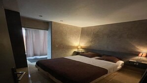 Quarto com uma cama grande, duas mesas de cabeceira com luminárias, uma porta e vista para uma janela com cortinas.