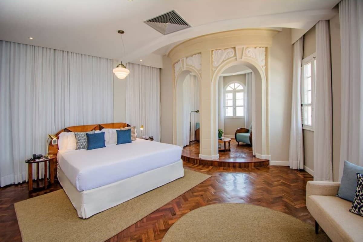 Um quarto espaçoso com uma cama grande, um espaço de estar com sofá e vista para um corredor.