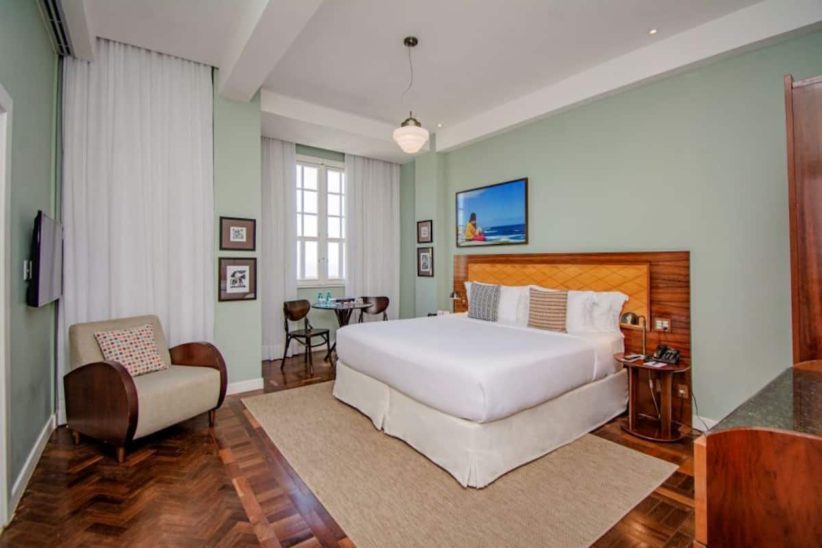 Quarto de hotel com uma cama grande, uma escrivaninha com cadeira, uma televisão e um quadro na parede.