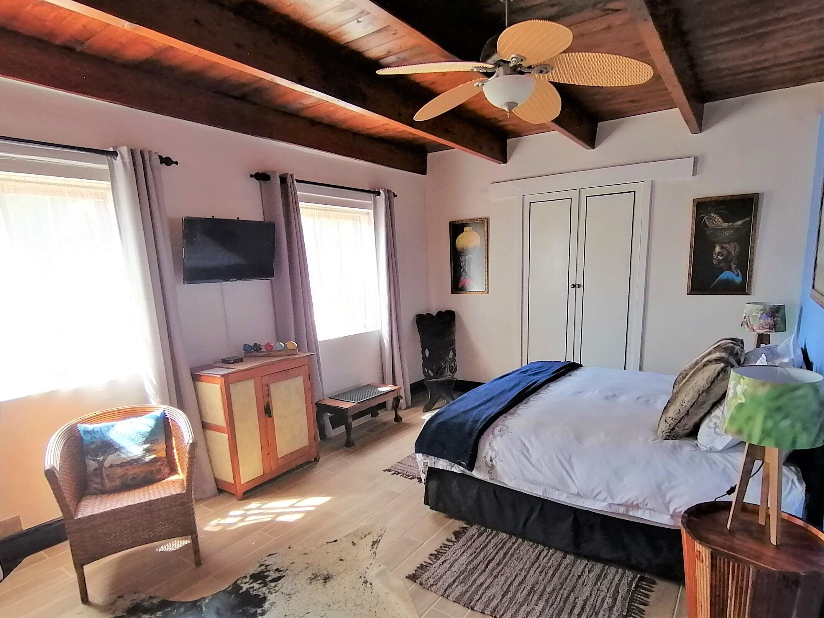 Quarto com cama, teto de madeira, ventilador de teto, TV, guarda-roupa, cadeira e mesa pequena.