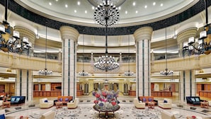 Um hall imponente com lustres elaborados, um arranjo floral central e várias áreas de estar.