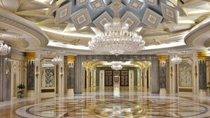 Um amplo saguão com um grande candelabro, teto ricamente decorado e piso de mármore polido.