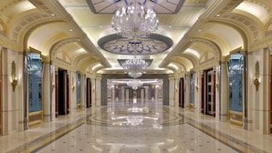 Um corredor imponente com piso espelhado, teto ricamente decorado e um lustre grande.
