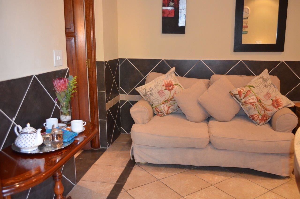 Um hall com um sofá bege, uma mesa lateral de madeira com uma bandeja de chá e um vaso de flores.