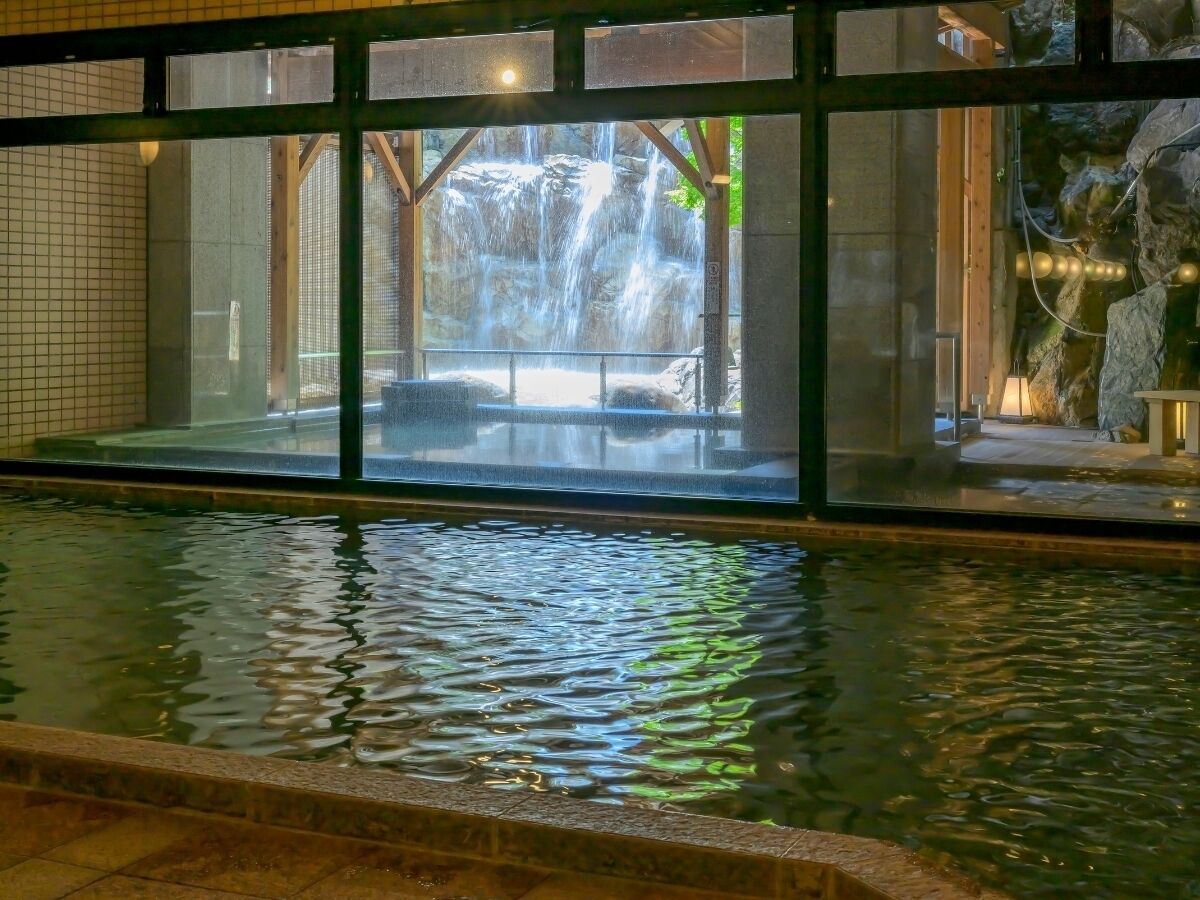 Uma área de piscina com uma cascata e um espaço de estar visível através de uma estrutura de vidro.