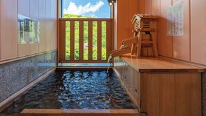 Uma onsen japonesa tradicional com interior em madeira, um banco de madeira e vista para o verde lá fora.