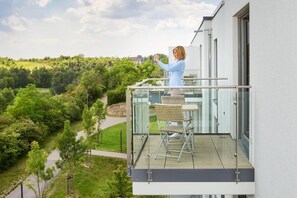 Varanda com guarda-corpo de vidro e vista para uma paisagem verde.