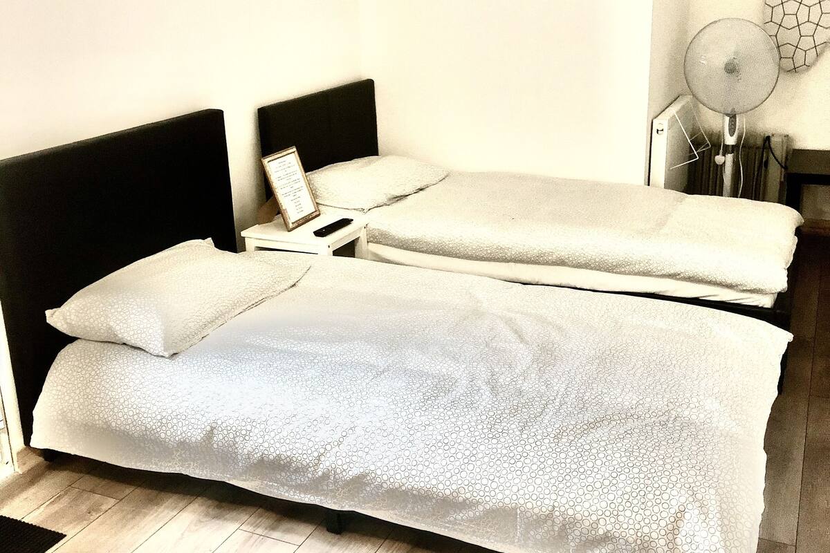 Uma cama de casal com colcha branca texturizada, cabeceira preta e mesa de cabeceira com abajur e uma moldura com foto.