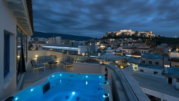 Terraço no telhado com banheira de hidromassagem, vista da cidade e um edifício com luz no topo.