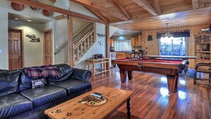 Uma sala de estar espaçosa com mesa de bilhar, sofá de couro e vigas de madeira no teto.