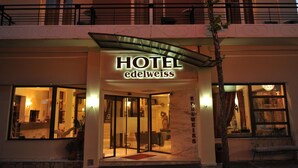 Entrada de hotel com porta de vidro, varanda com grades e uma placa com a inscrição "HOTEL adelweiss".