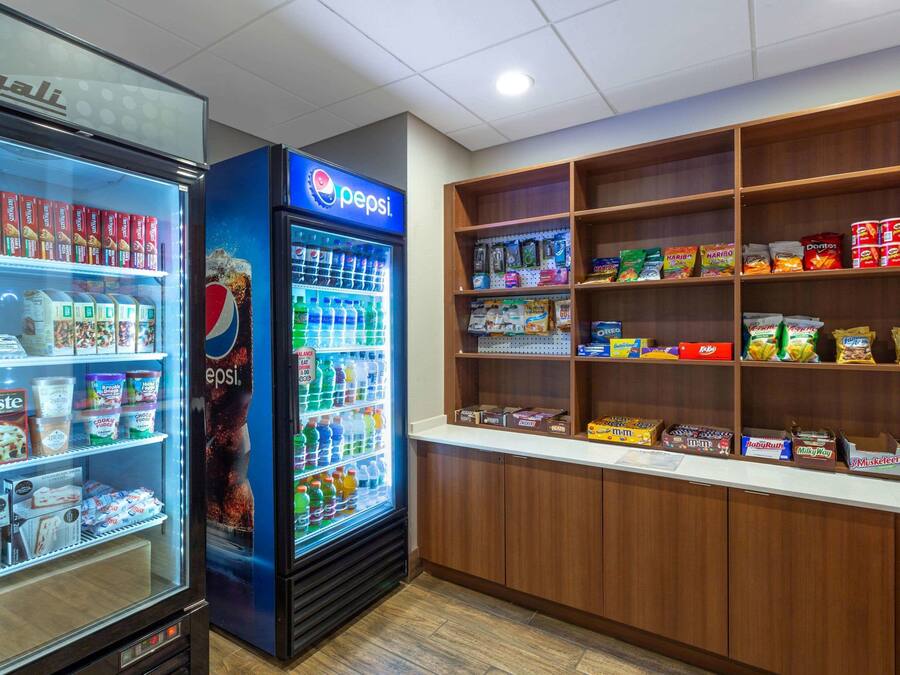 Uma área com máquinas de venda automática, incluindo um refrigerador da Pepsi, e uma prateleira repleta de lanches e bebidas.
