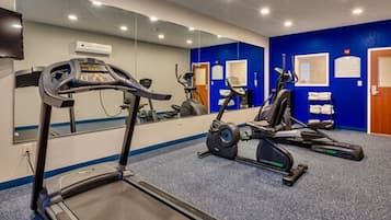 Academia com equipamentos de cardio, espelho e parede azul com porta.
