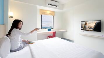Quarto de hotel com cama, televisão na parede, janela com vista e uma cadeira vermelha.