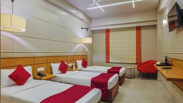 Quarto de hotel com três camas, uma escrivaninha, uma cadeira, uma televisão e uma janela com detalhe em vermelho.