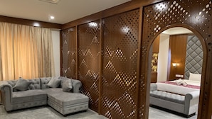 Quarto de hotel moderno com um sofá seccional cinza, cama com encosto cinza e um painel de madeira decorativo com padrões perfurados.