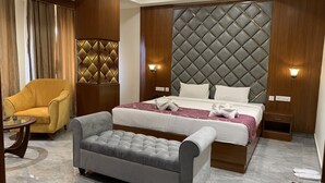 Quarto de hotel moderno com uma cama grande, um sofá, uma mesinha e um painel decorativo na parede.