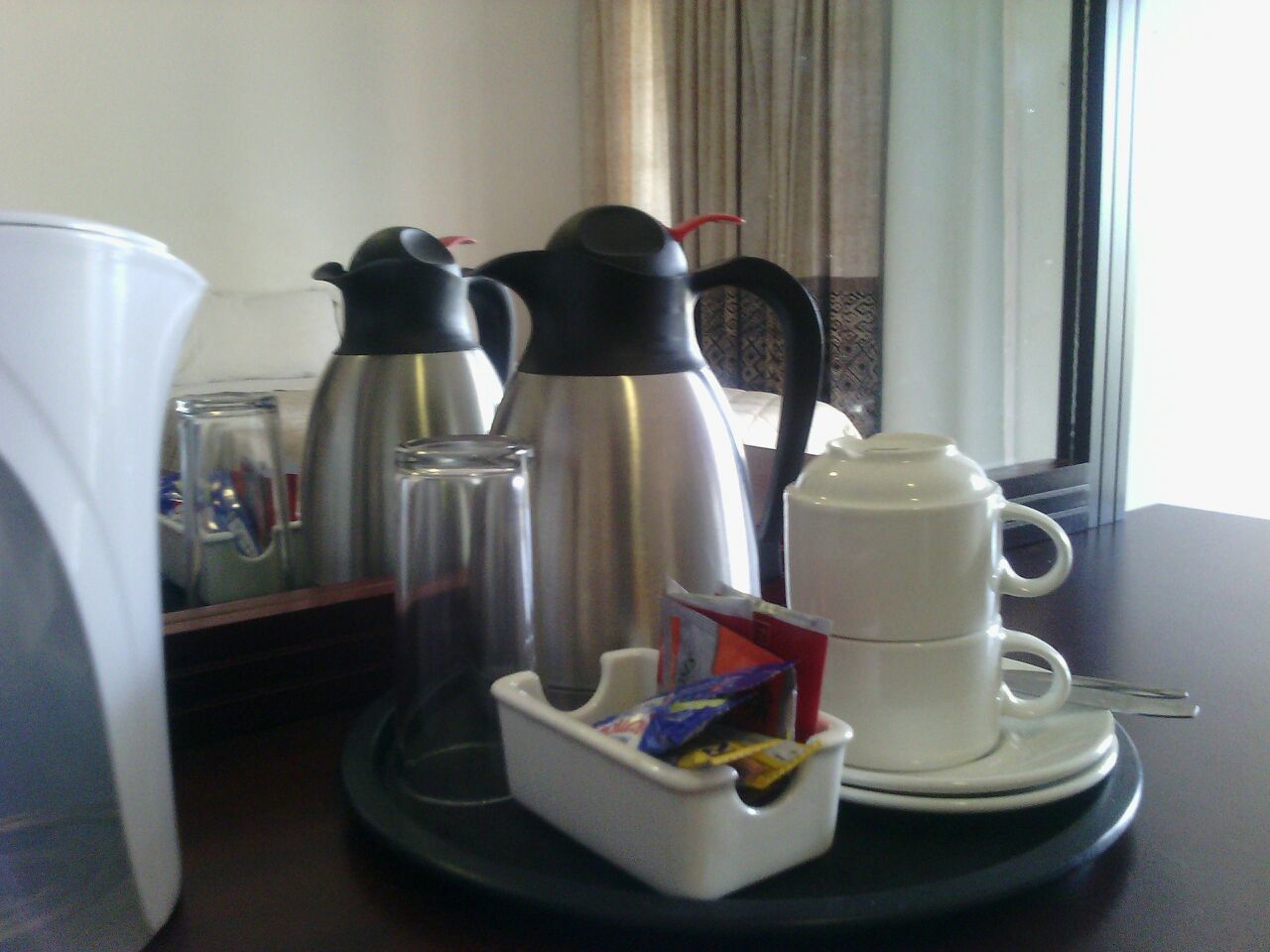 Disposição para o café da manhã, com cafeteira, bule e xícara e pires em uma bandeja.