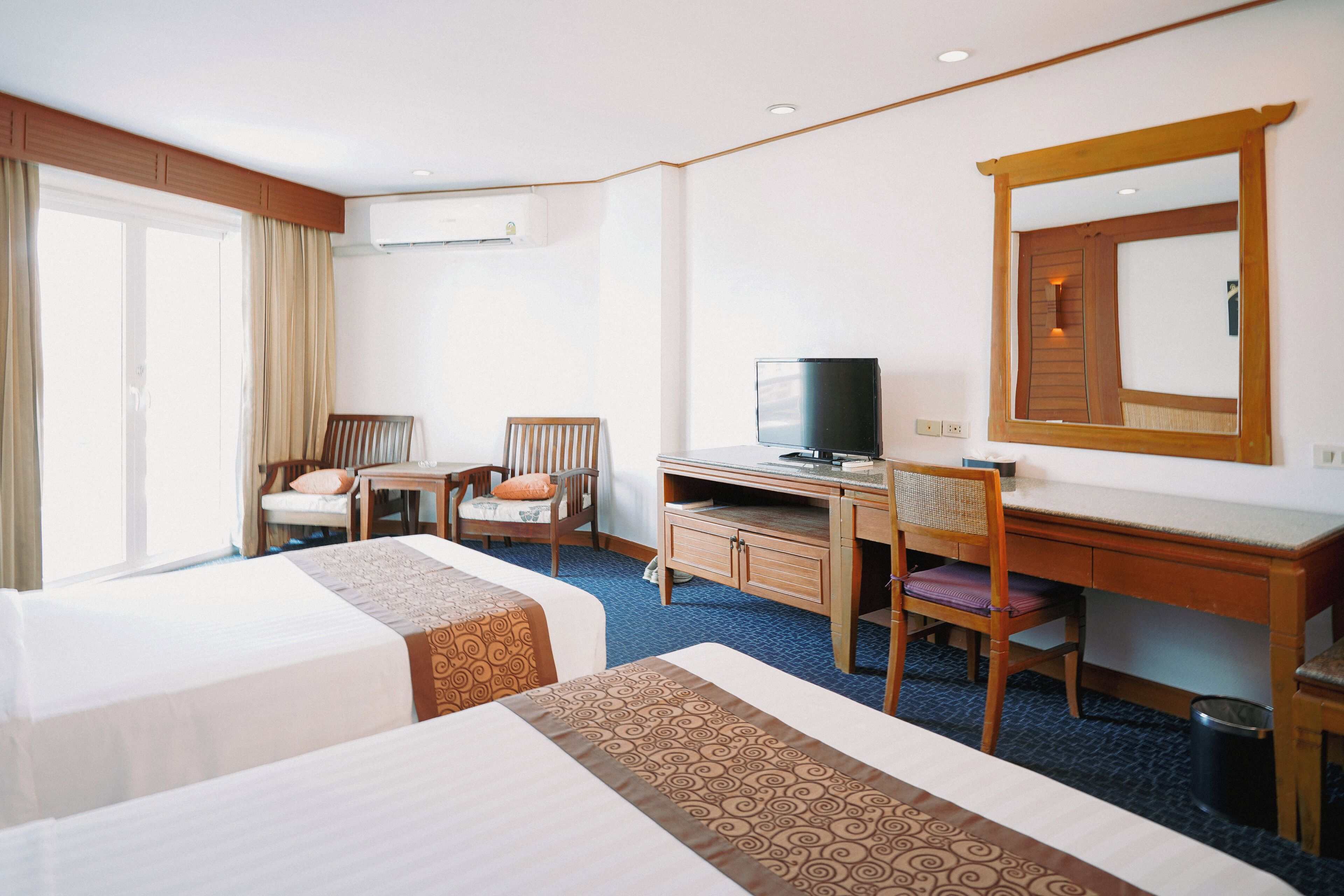 Quarto de hotel com duas camas, uma mesa de trabalho, televisão, uma cadeira e um espelho grande na parede.