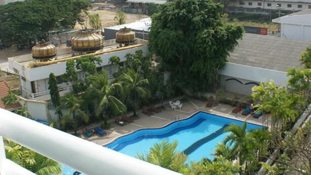 Área de piscina no terraço, com palmeiras e vista para edifícios ao redor.