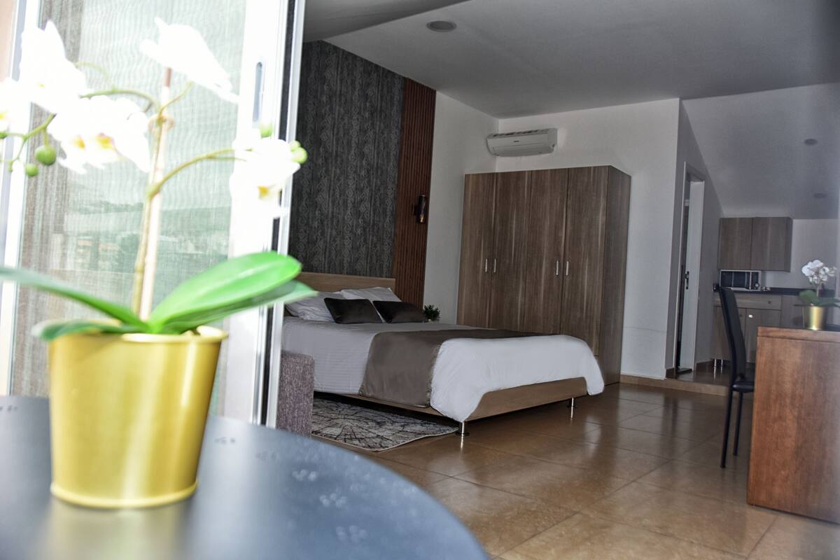 Quarto moderno com cama, guarda-roupa de madeira e uma pequena área de cozinha.
