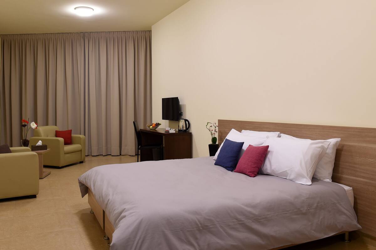 Quarto de hotel com cama, escrivaninha, cadeira, televisão e janela com cortinas.