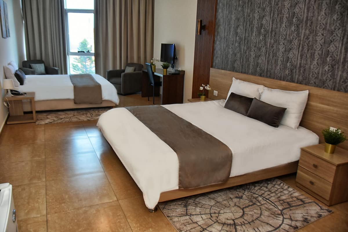Quarto de hotel com duas camas, uma escrivaninha, uma cadeira, televisão e vista para o exterior.