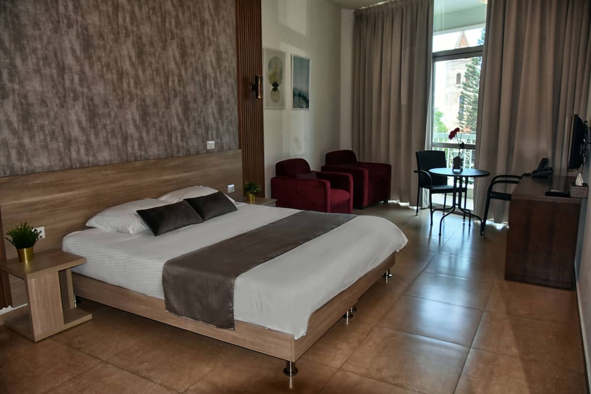 Quarto de hotel moderno com uma cama grande, uma escrivaninha, duas cadeiras e vista para um edifício pela janela.