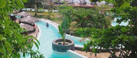 Uma área de piscina com um elemento aquático curvo, rodeada por palmeiras e espreguiçadeiras.